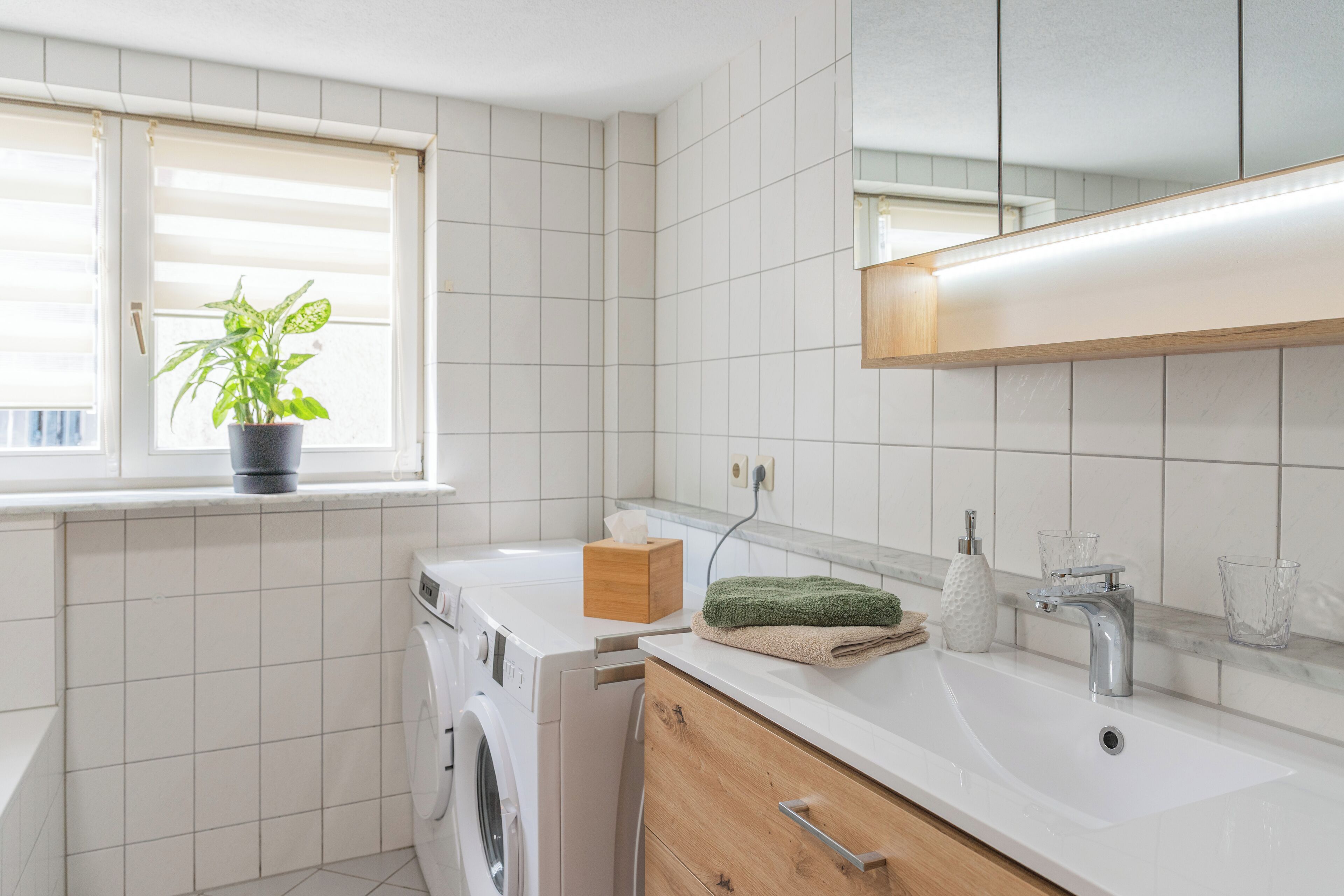 Uma casa de banho moderna com máquina de lavar roupa, lavatório com espelho e janela com planta em vaso.