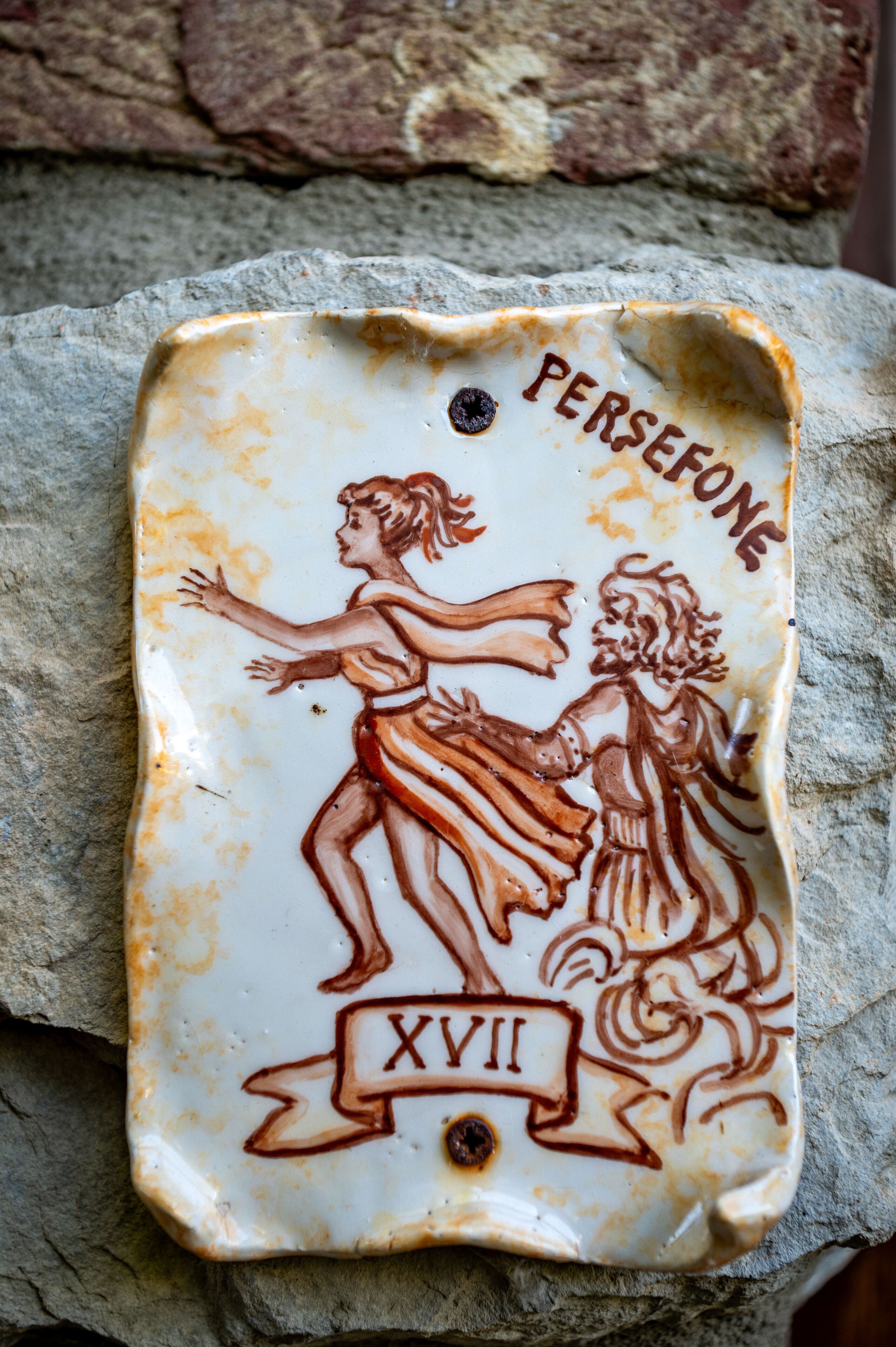 Um azulejo de cerâmica com uma figura e a inscrição 'PERSEFONE' e 'XVII'.