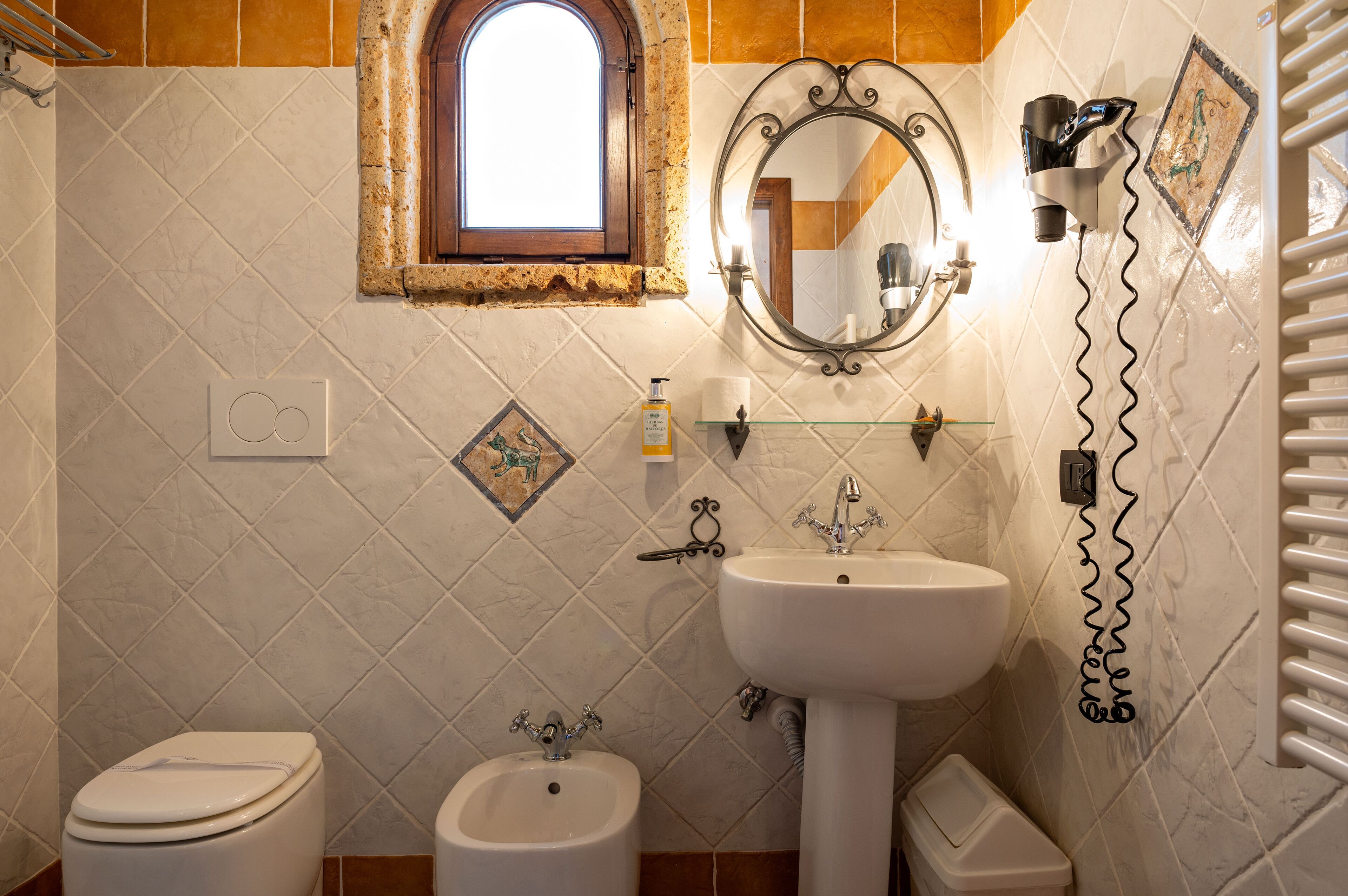 Casa de banho com sanita, bidé, lavatório e secador de cabelo fixado na parede.