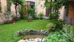 Um pequeno jardim com lago, um banco de madeira e diversas plantas.