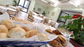 Uma área de refeições com mesas preparadas para uma refeição, com cestos de pão e doces.