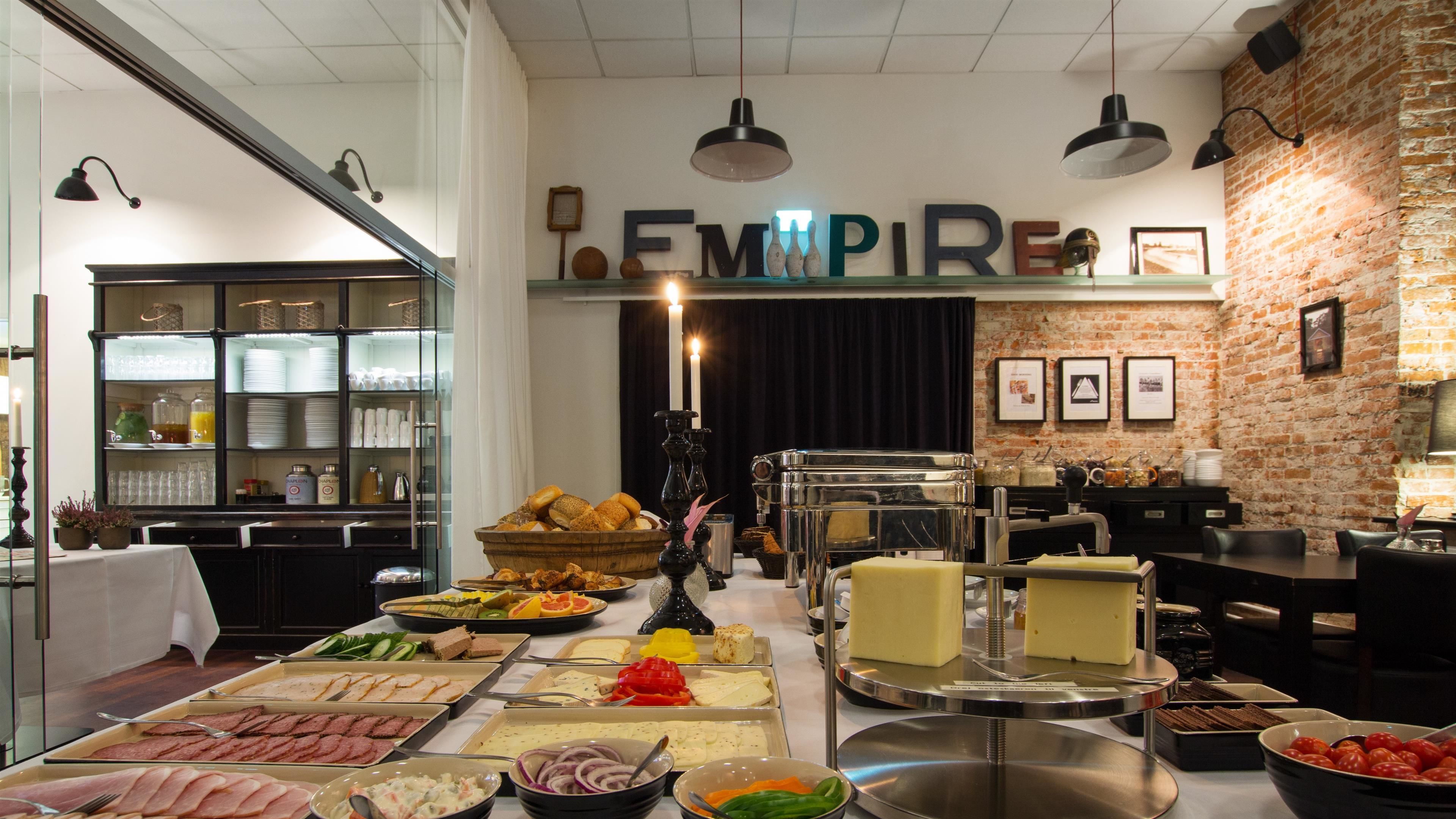 Disposição de buffet com diversos tipos de comida e uma parede de tijolos com a palavra "EMPIRE" em cima.