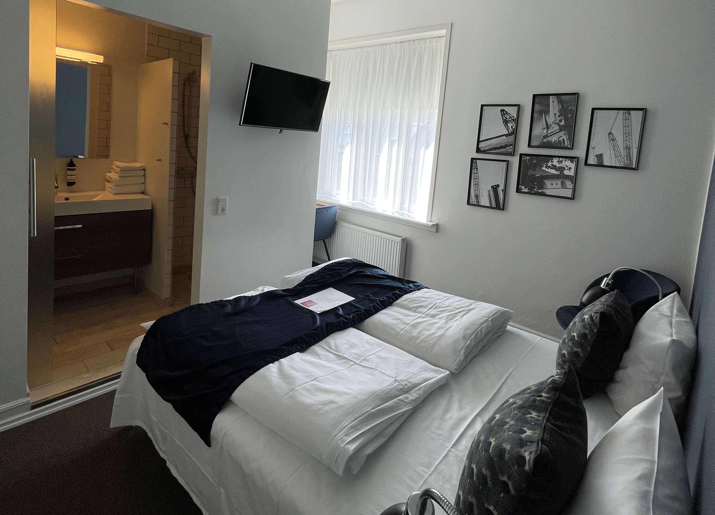 Quarto com cama, TV na parede e janela com cortinas.