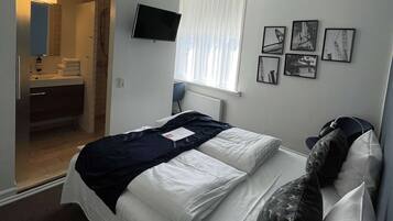 Quarto com cama, TV na parede e janela com cortinas.