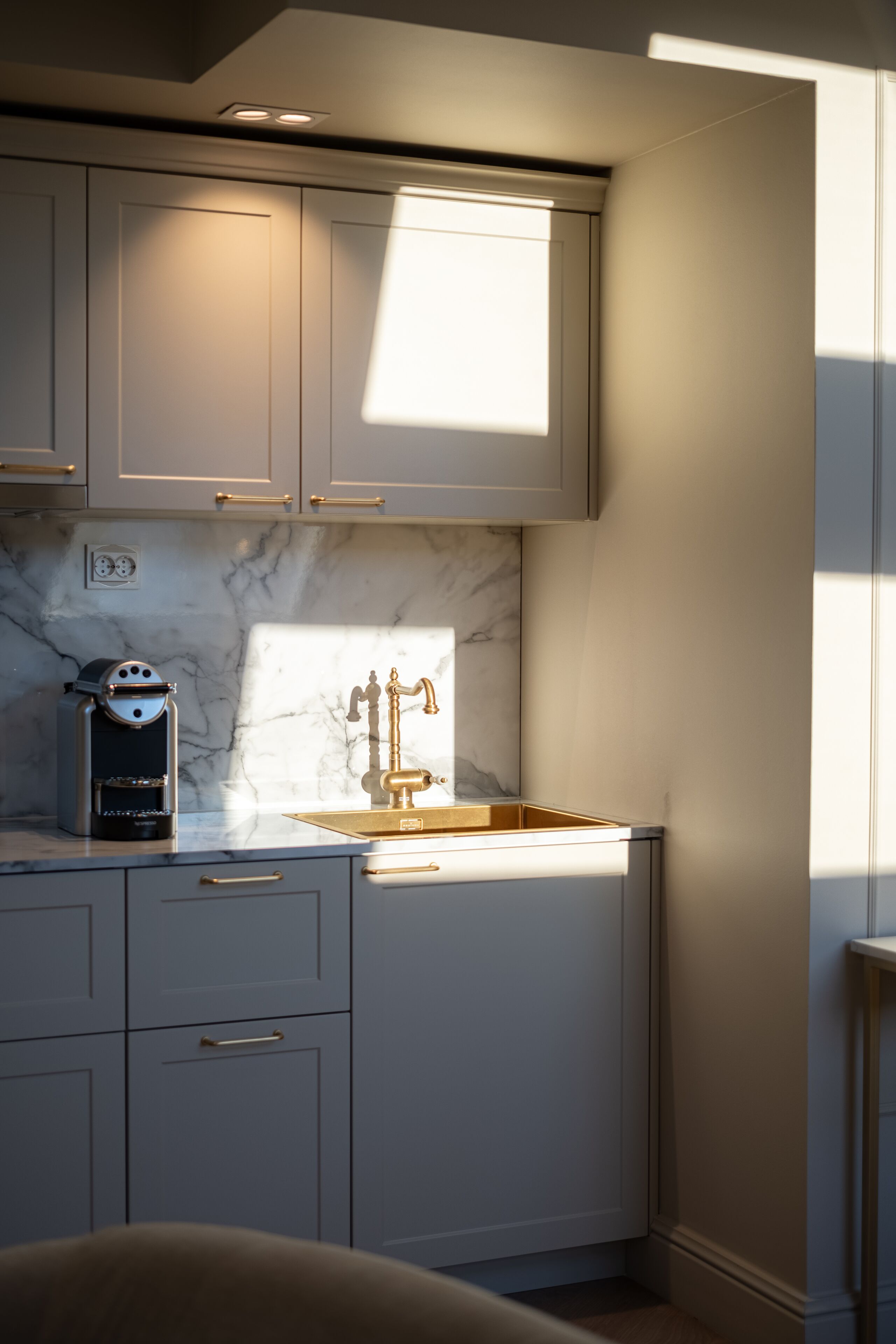 Cozinha moderna com bancadas de mármore, máquina de café integrada e torneira dourada.