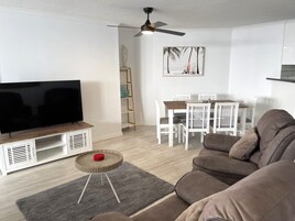 Uma sala de estar moderna com televisão de tela plana, um sofá marrom, uma mesa de jantar com cadeiras e um ventilador de teto.