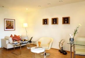Uma sala de estar moderna com sofá, poltrona, mesa de centro e uma mesa de vidro com um laptop.
