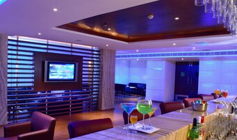Uma área de bar moderna com uma mesa comprida, banquetas e uma tela de televisão.