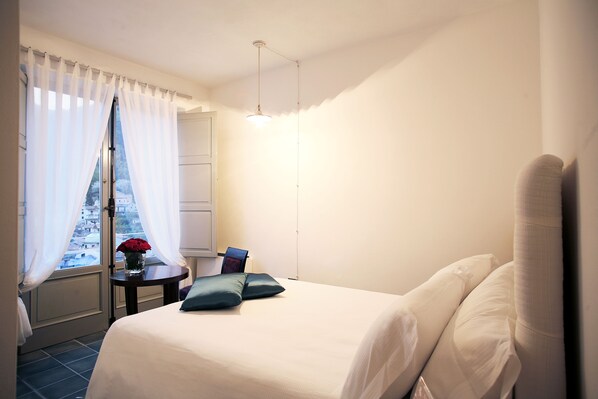 Quarto de hotel com cama, uma mesinha com um vaso de flores e vista para a cidade pela janela.