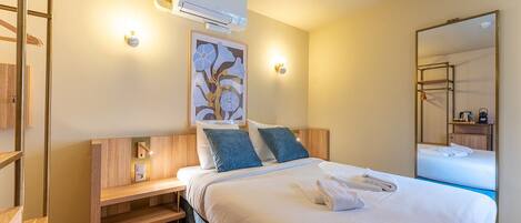 Quarto de hotel com cama, mesas de cabeceira, ar condicionado, espelho fixado na parede e um quadro.