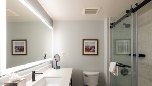 Uma casa de banho moderna com um espelho grande, uma sanita, uma pia e cabine de duche em vidro.