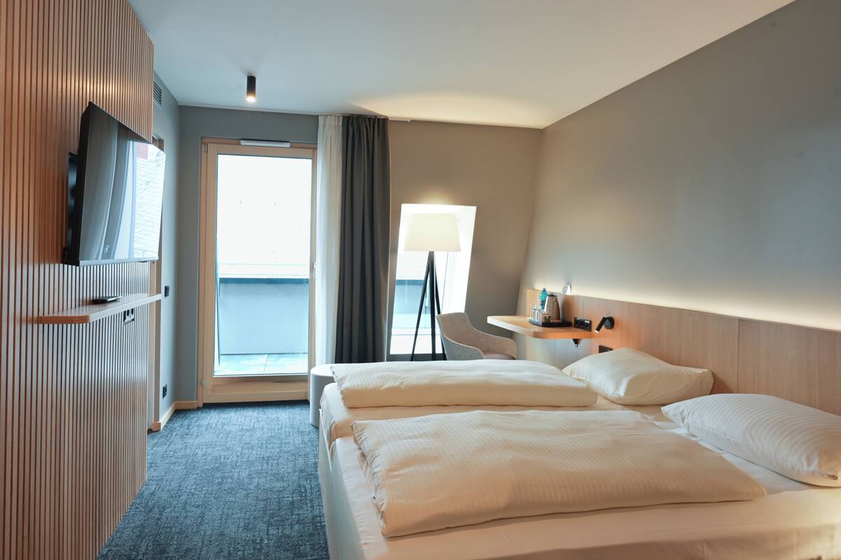 Quarto de hotel com duas camas, uma escrivaninha, uma cadeira, televisão e vista para o mar.