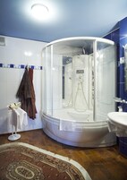 Uma casa de banho moderna com chuveiro em cabine de vidro, lavatório branco e tapete estampado no chão.
