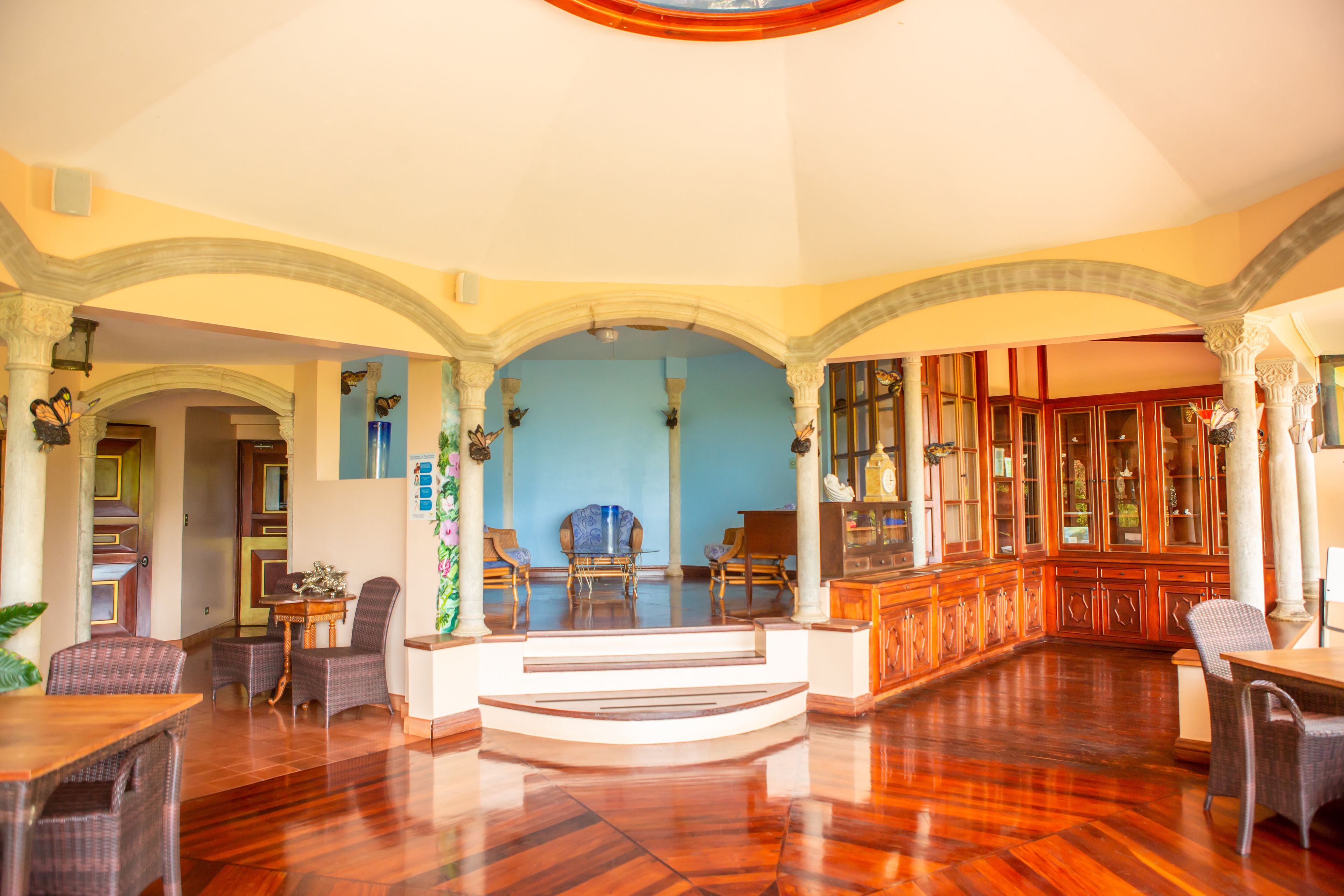 Interior espaçoso com teto alto, colunas ornamentadas e escadaria central que leva a um andar superior.