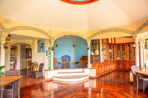 Interior espaçoso com teto alto, colunas ornamentadas e escadaria central que leva a um andar superior.