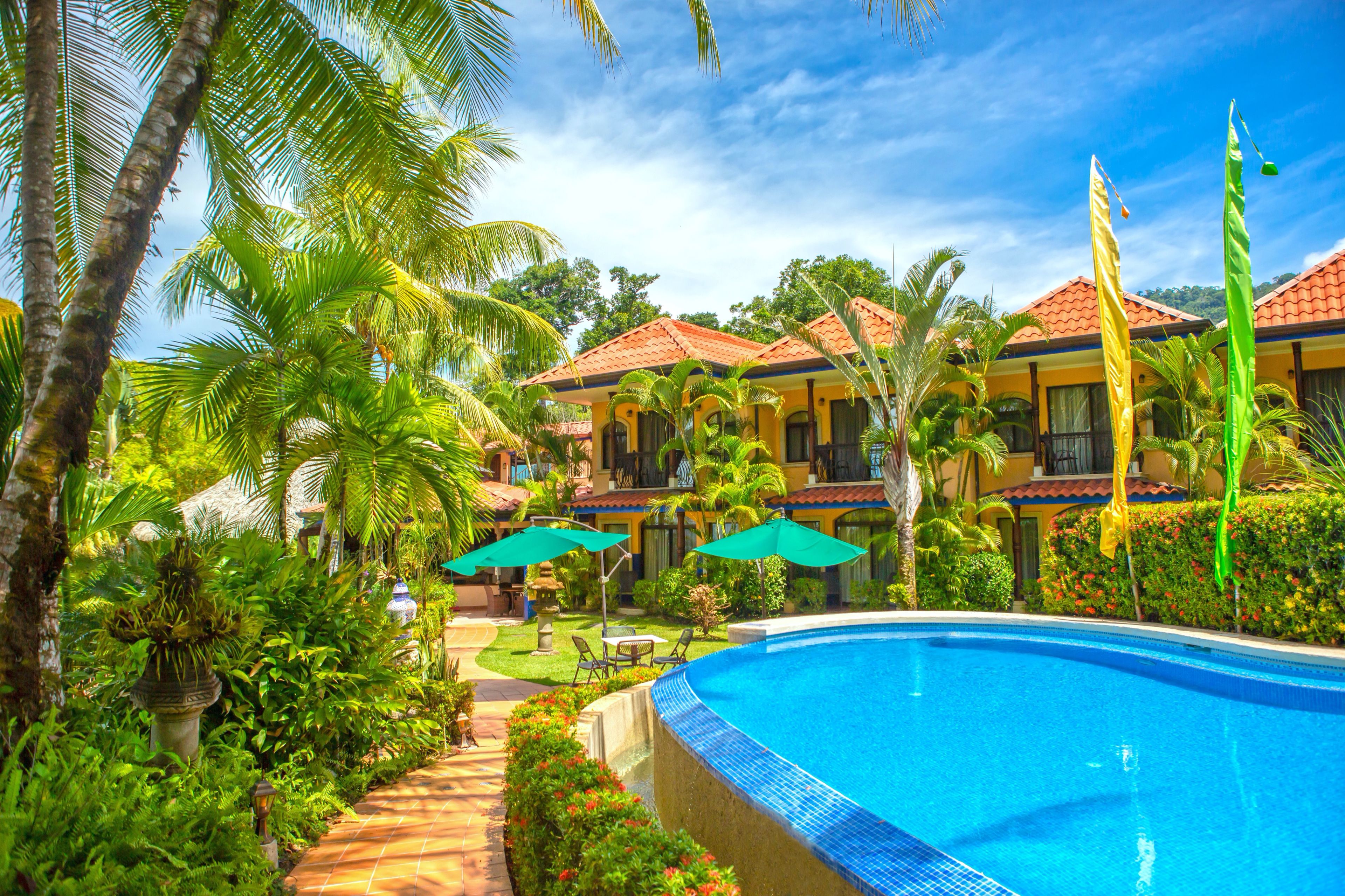 Resort com piscina, palmeiras e um prédio com telhado de telhas vermelhas.