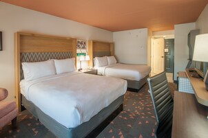 Quarto de hotel com duas camas, uma escrivaninha, uma cadeira e uma porta que dá para outro aposento.
