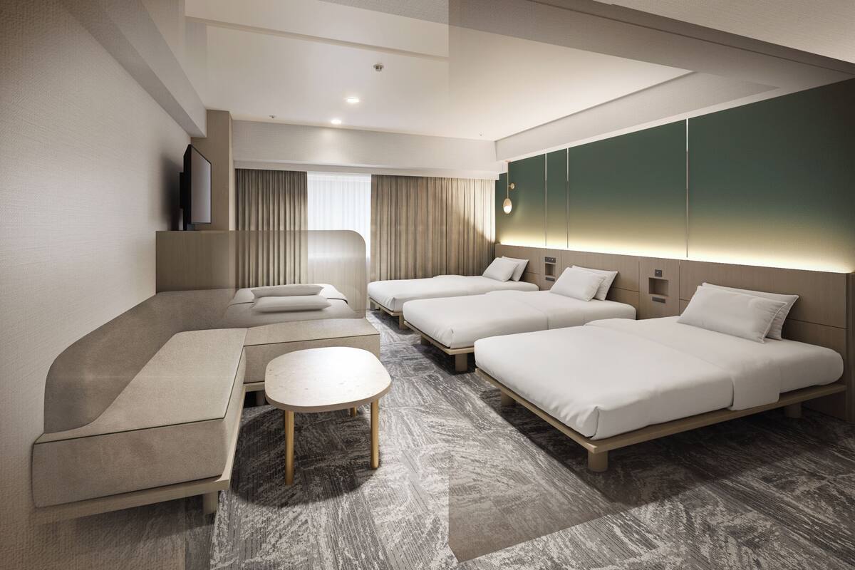Quarto de hotel moderno com sofá, duas camas de solteiro, uma pequena mesa e televisão.