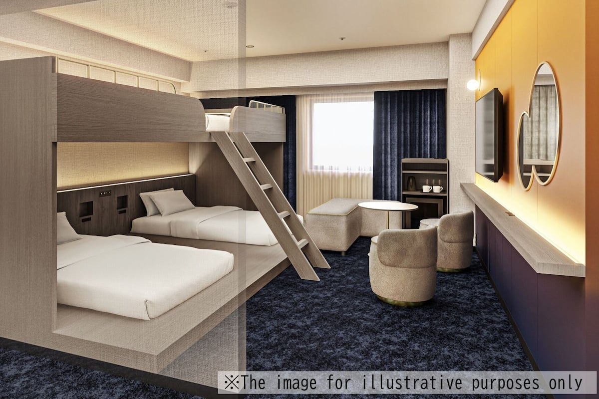 Quarto de hotel com cama beliche, escrivaninha, cadeira, mesa pequena e espelho.