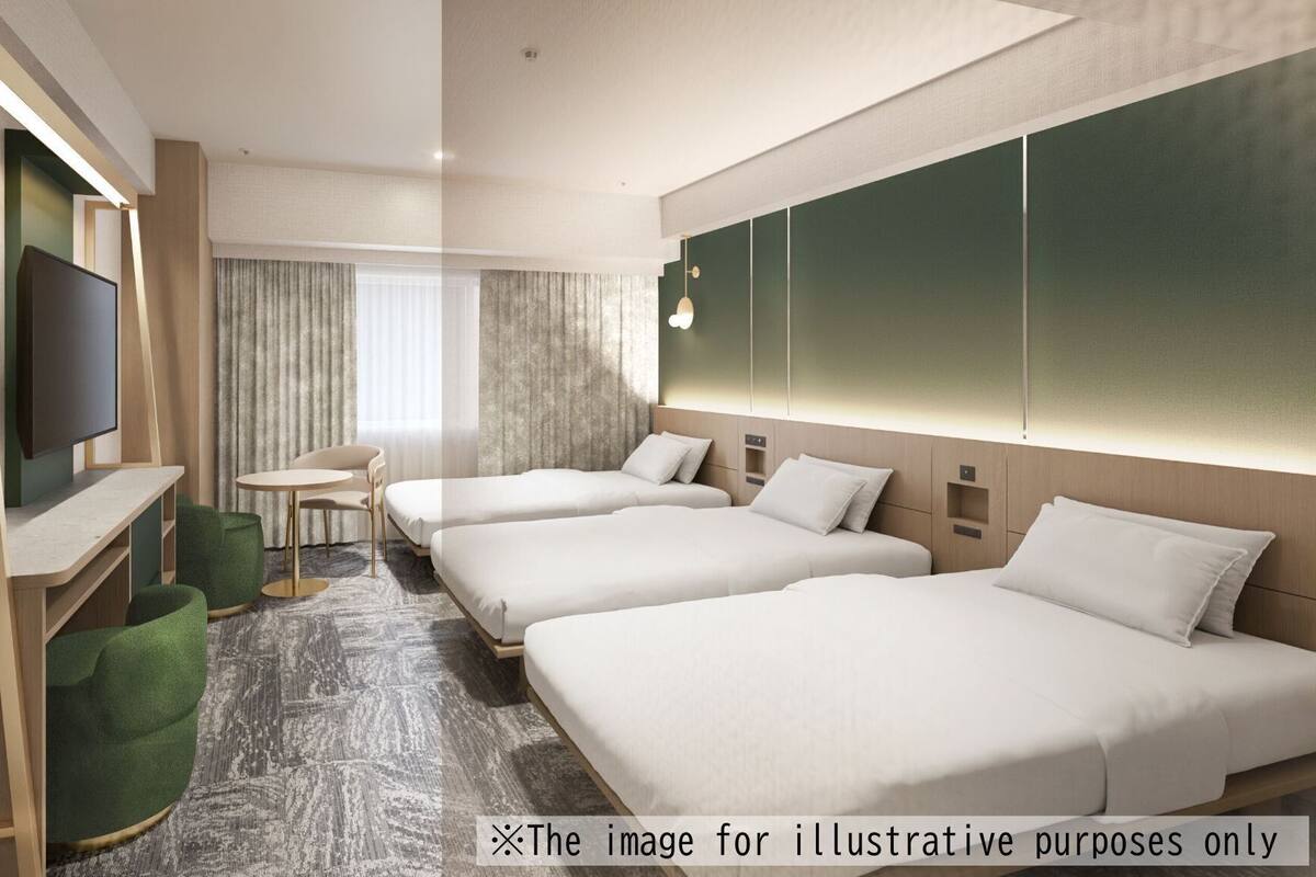 Quarto de hotel com três camas, televisão, uma pequena mesa e uma cadeira verde.