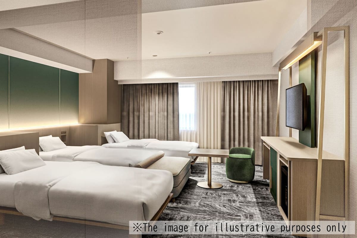 Quarto de hotel com duas camas, uma televisão, uma mesinha e uma cadeira verde.