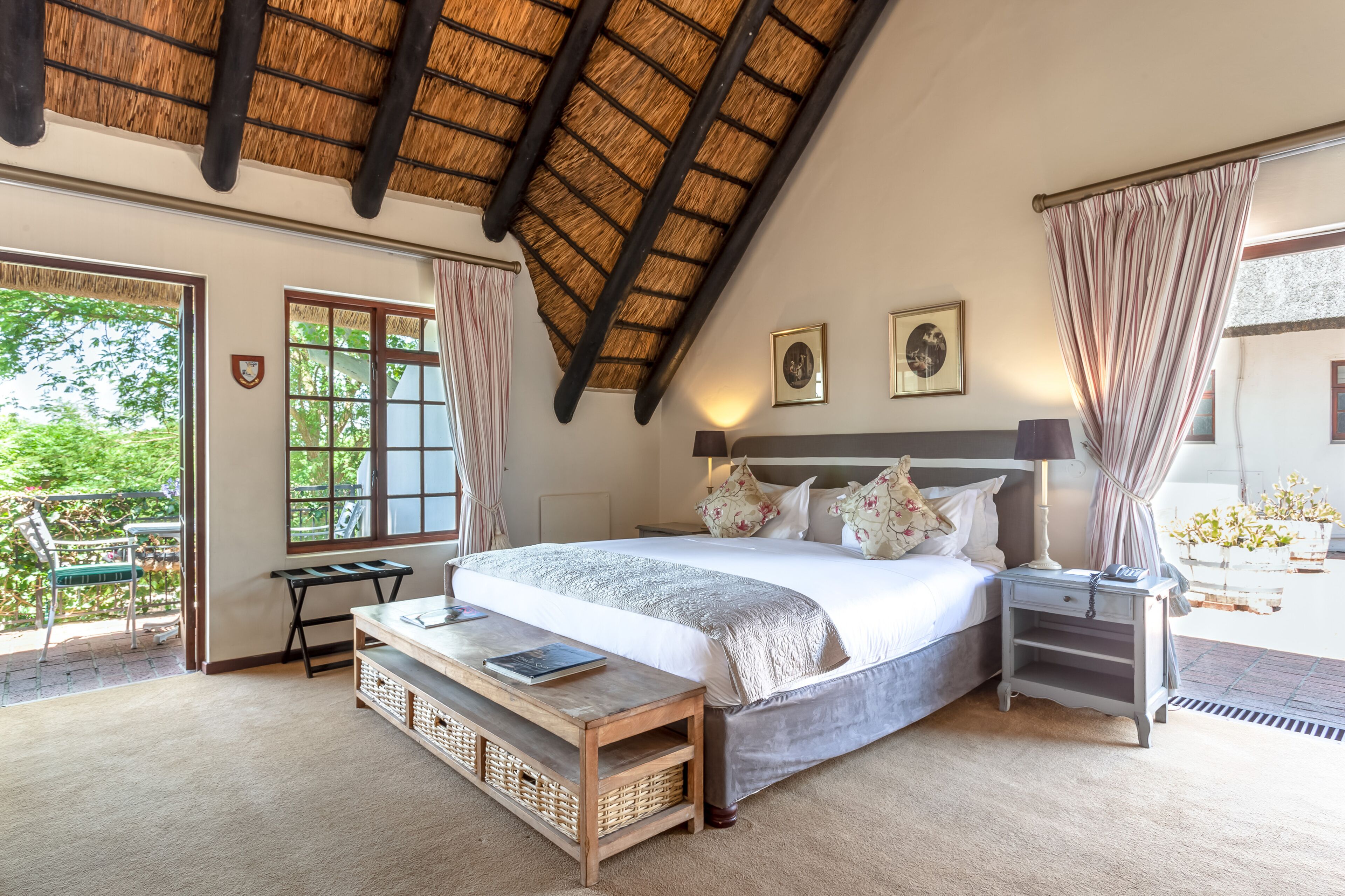 Um quarto com uma cama grande, uma mesinha de cabeceira, um banco e uma janela com cortinas.