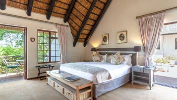 Um quarto com uma cama grande, uma mesinha de cabeceira, um banco e uma janela com cortinas.