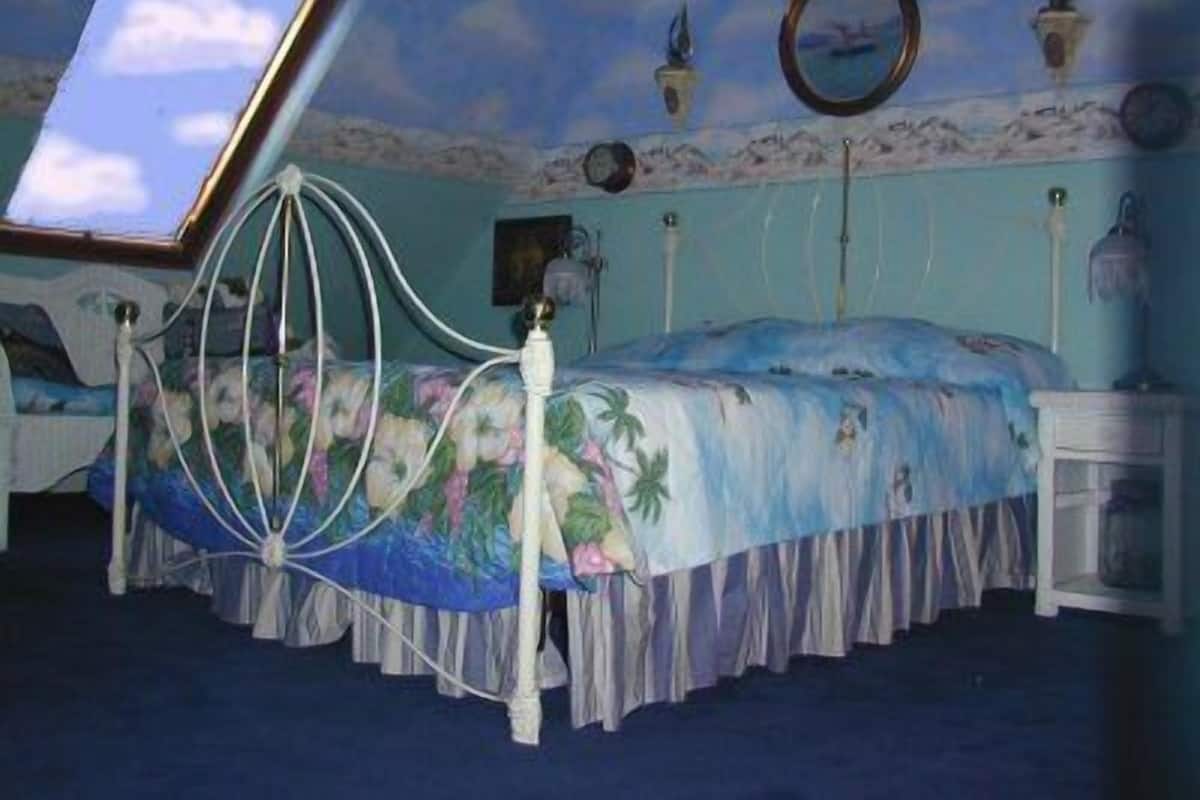 Quarto com cama, mesa de cabeceira, espelho e janela.
