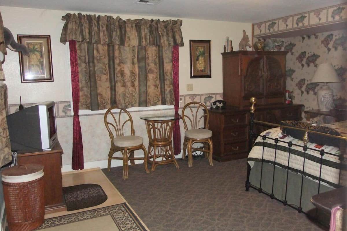 Uma sala de estar com televisão, duas cadeiras, uma mesinha, um armário e uma cama.