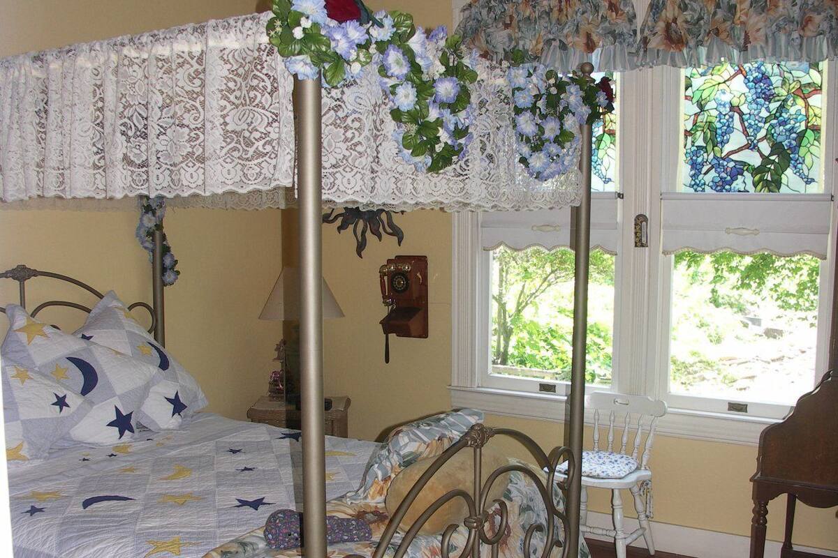 Uma cama com dossel adornada com colchas florais, um baldaquim de renda e uma câmera antiga na mesa de cabeceira.