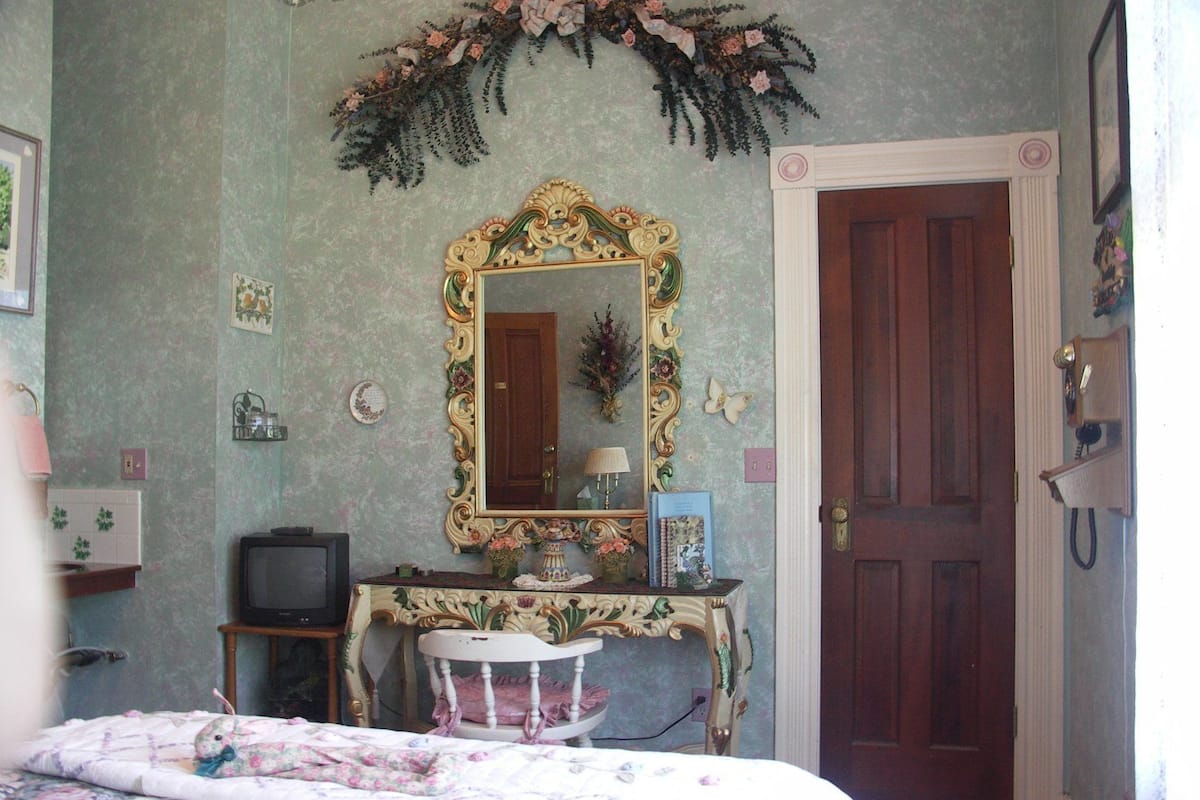 Quarto com cama, cómoda, espelho e porta.