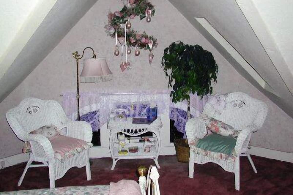 Um quarto de sótão aconchegante com duas cadeiras de vime brancas, uma mesa pequena e uma planta grande.