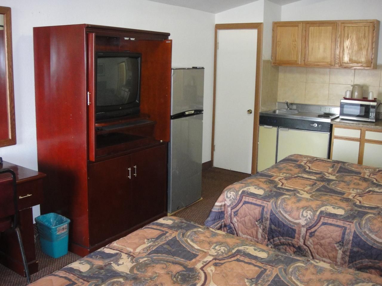 Quarto de hotel compacto com cama, cozinha compacta, armário de madeira com televisão e lixeira.
