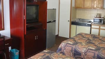 Quarto de hotel compacto com cama, cozinha compacta, armário de madeira com televisão e lixeira.
