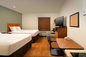 Quarto de hotel com duas camas, uma escrivaninha, uma cadeira, televisão e janela com persianas.
