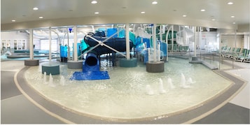 Parque aquático interno com um tobogã central, várias fontes e áreas de estar.