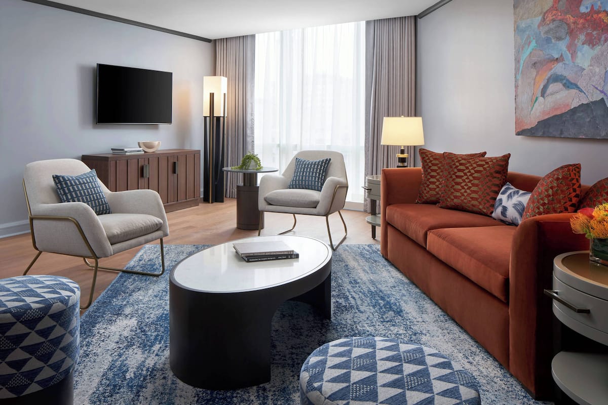 Quarto de hotel moderno com uma cama, duas poltronas, um sofá, uma mesa de centro e uma televisão.