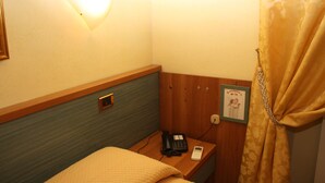Quarto de hotel com uma cama, uma mesa de cabeceira com telefone, uma luminária na parede e um quadro emoldurado.