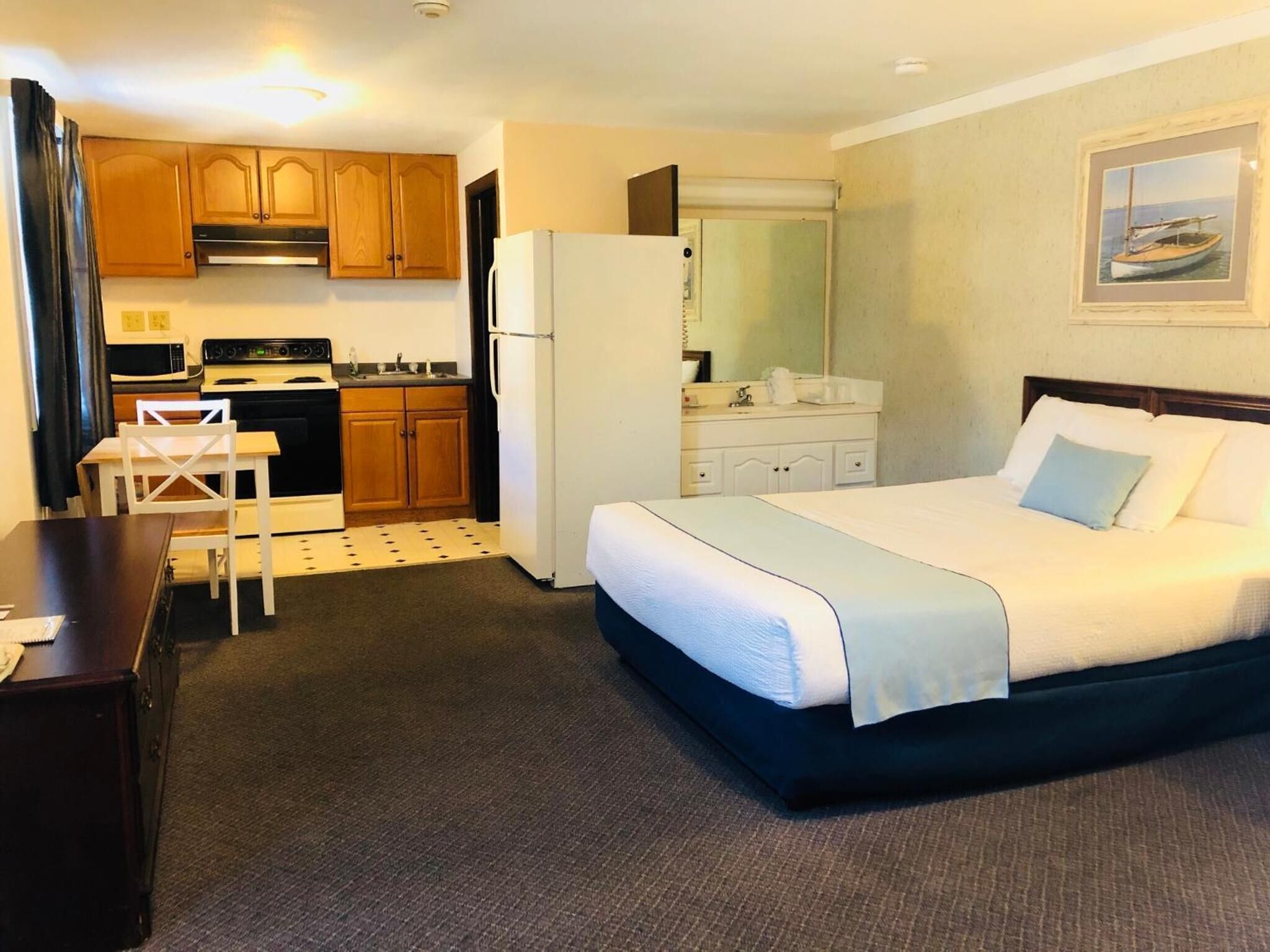 Quarto de hotel com cama, escrivaninha, cadeira, cozinha compacta e banheiro.