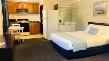 Quarto de hotel com cama, escrivaninha, cadeira, cozinha compacta e banheiro.