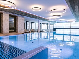 Piscina interior moderna com vista clara para a piscina, área de estar e grandes janelas.