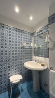 Um banheiro com azulejos azuis e brancos estampados, uma pia de pedestal, um espelho e um banquinho branco.