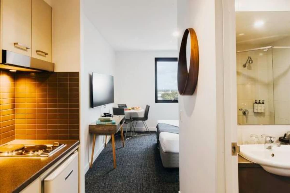 Quarto de hotel compacto com cozinha compacta, área de refeições, cama e banheiro.