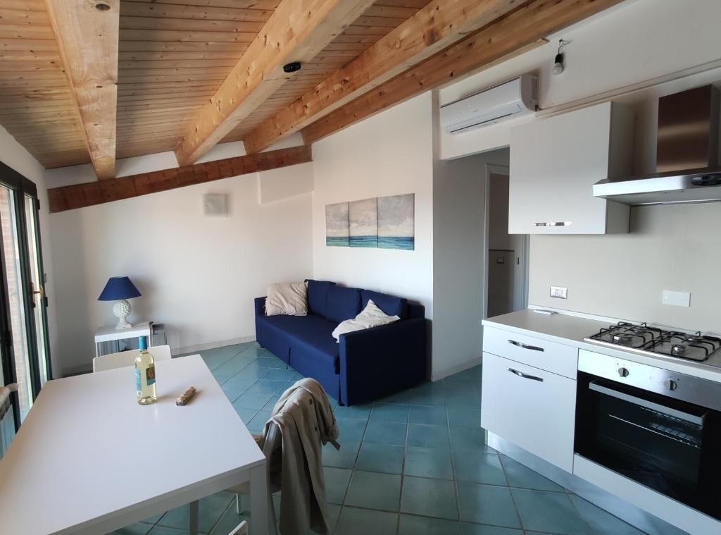 Cozinha moderna com armários brancos e fogão a gás, sofá azul e mesa de jantar com luminária.