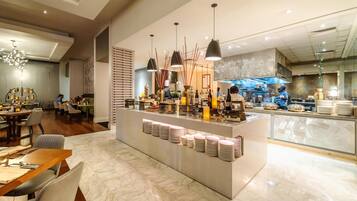 Um restaurante moderno com chão de mármore, um balcão de atendimento central e uma área de cozinha ao fundo.
