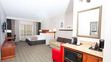 Quarto de hotel com cama, secretária, sofá, máquina de café e micro-ondas.