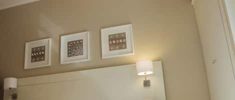 Quarto de hotel com uma cama, uma mesa de cabeceira e três obras de arte emolduradas na parede.
