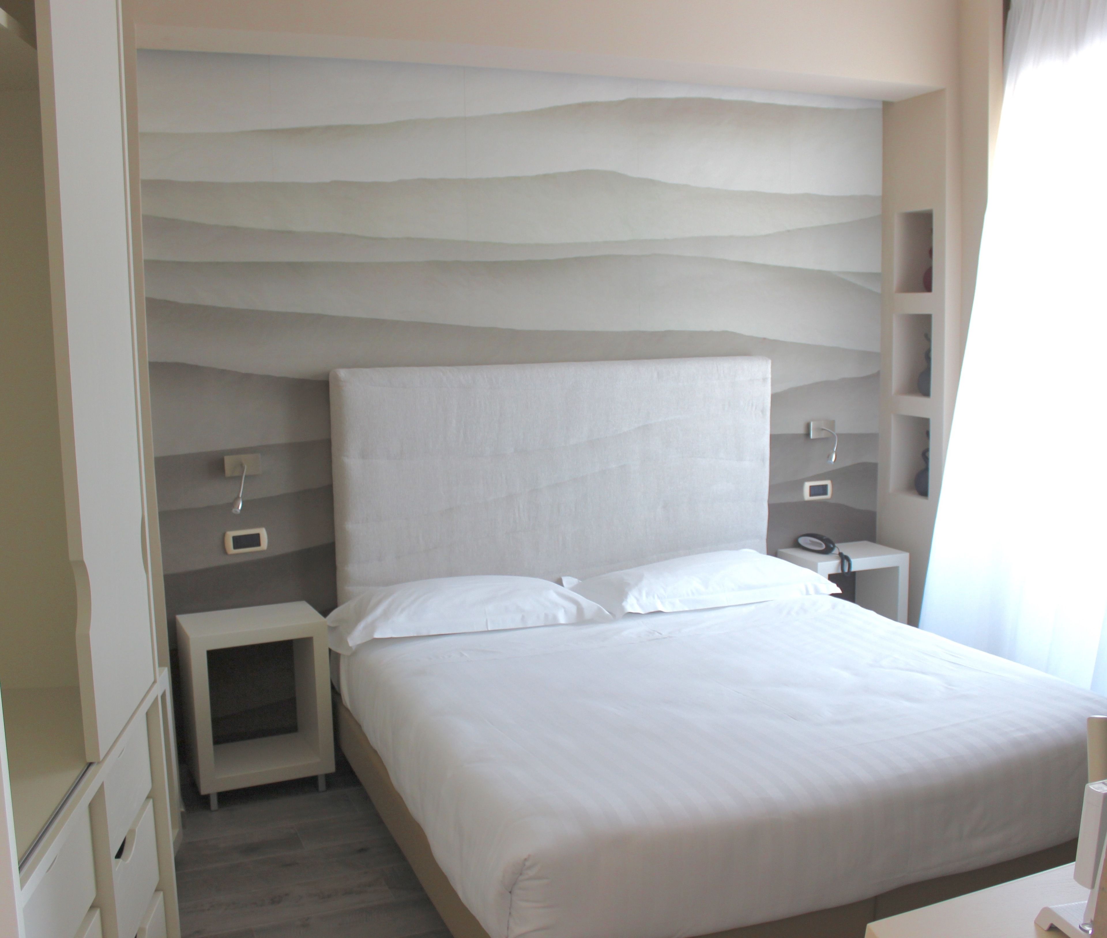 Quarto com cama grande, mesa de cabeceira e prateleira na parede.