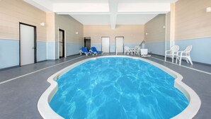 Piscina interna com um recurso aquático azul, rodeada por espreguiçadeiras e uma área de estar.