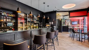Uma área de bar com balcão, várias luminárias pendentes e uma variedade de garrafas e copos nas prateleiras.